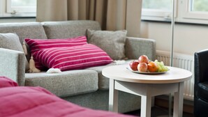 Uma sala de estar moderna com um sofá cinzento, uma mesa redonda branca com frutas e um abajur.