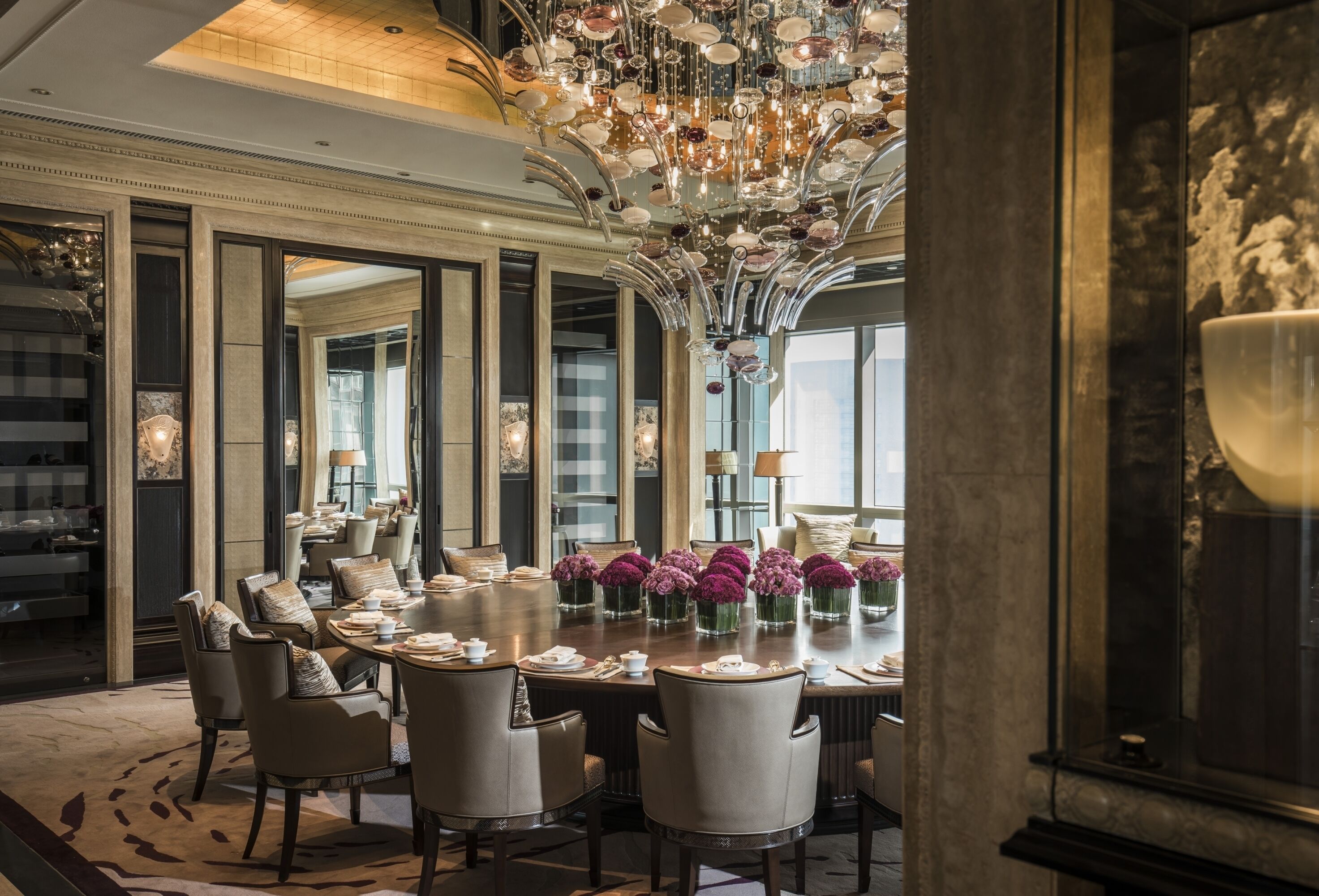 Uma sala de jantar formal com uma mesa comprida, cadeiras elegantes e um lustre.