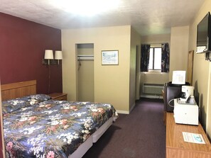 Quarto de hotel com cama, escrivaninha, espelho, janela com cortinas e pequena área de cozinha.