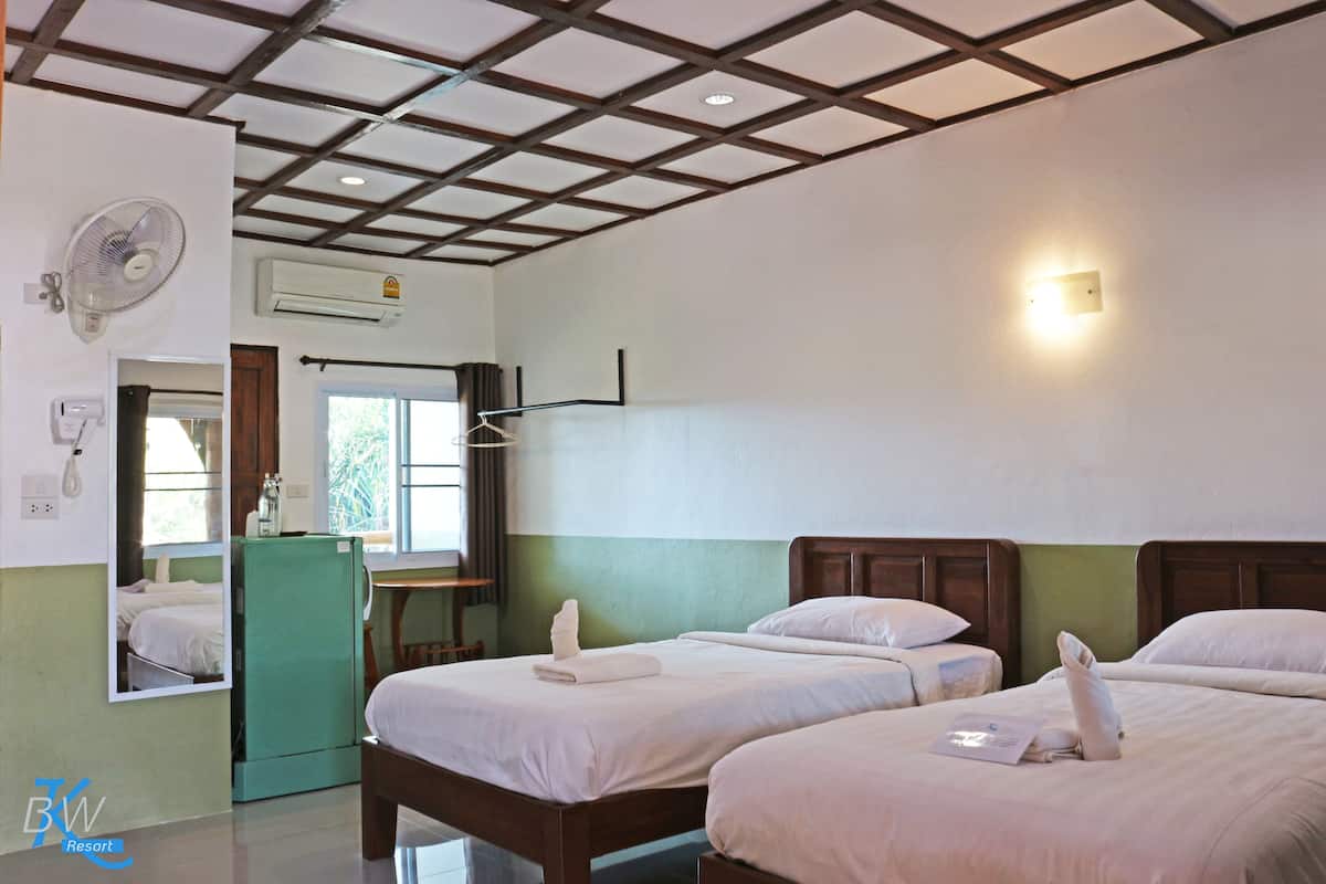 Quarto de hotel com duas camas, espelho, ventoinha, ar condicionado e janela com vista para o verde.