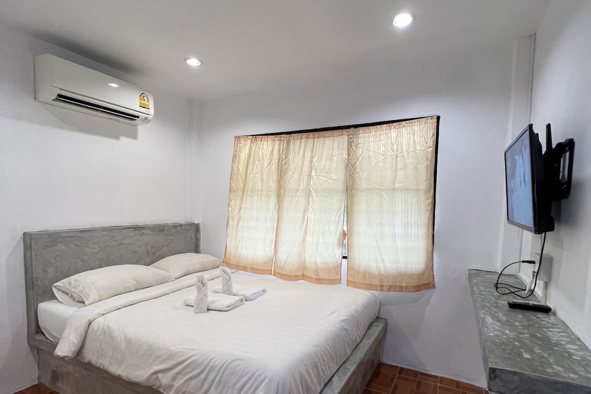 Quarto com cama, ar condicionado, televisão e janela com cortinas.