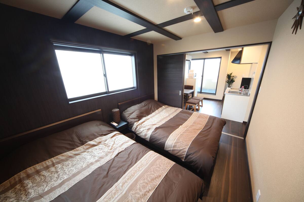 Quarto com duas camas, uma mesinha e uma janela.