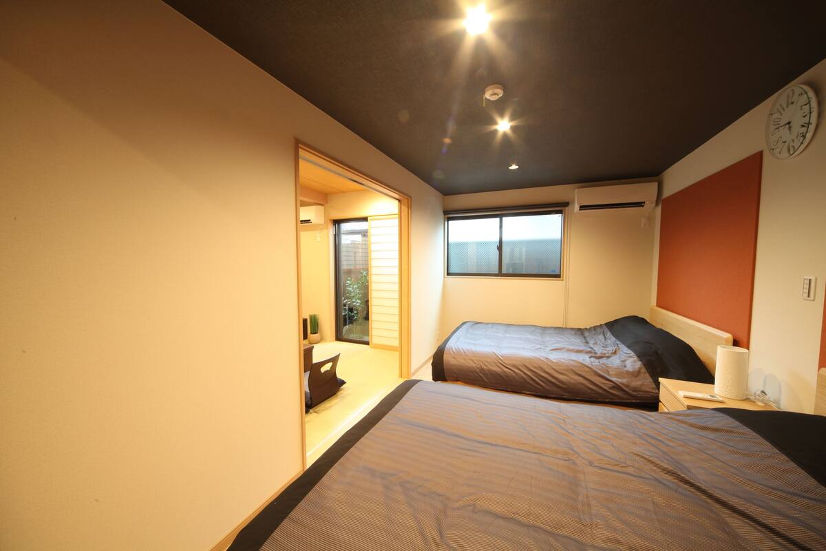 Quarto com duas camas, janela, aparelho de ar condicionado e relógio na parede.