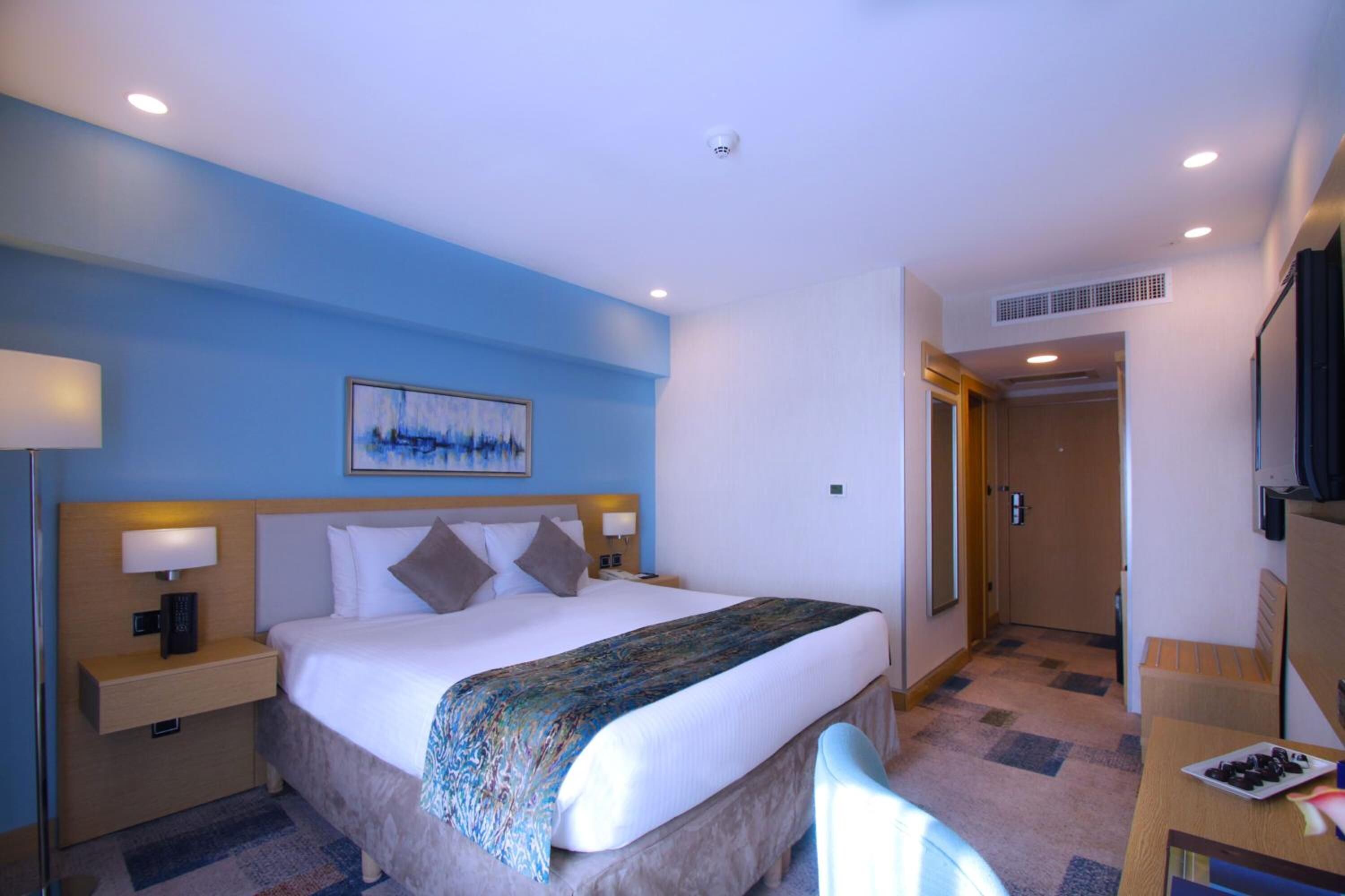 Quarto de hotel com cama, mesas de cabeceira, escrivaninha e uma cadeira.