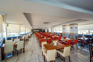 Uma sala de jantar ampla com várias mesas e cadeiras, janelas grandes e um design moderno e limpo.