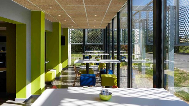 Uma sala de jantar moderna e arejada, com mesas e cadeiras, grandes janelas e vista para o exterior.