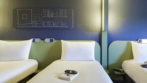 Quarto de hotel com duas camas, uma obra de arte na parede e uma mesa de cabeceira com um livro e óculos.