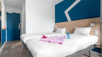 Quarto de hotel com uma cama grande, roupa de cama branca, parede azul com design geométrico e cabeceira de madeira.
