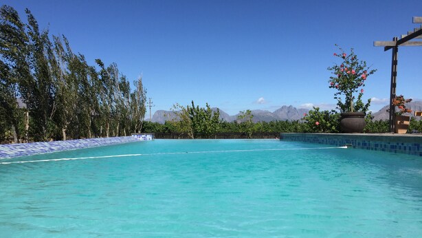 Piscina azul límpida com borda em azulejo, rodeada por vegetação exuberante e vista para montanhas ao fundo.