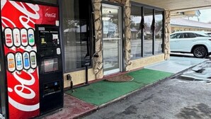 Máquina de Coca-Cola do lado de fora de um prédio com porta e janelas de vidro.