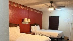 Quarto de hotel com duas camas, um ventilador de teto, um abajur e uma janela com persianas.