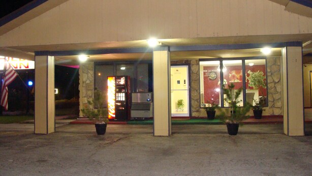 Um edifício com entrada coberta, plantas em vasos e uma máquina de refrigerantes Coca-Cola.