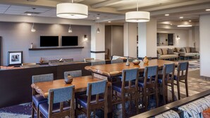Uma sala de jantar de hotel com uma longa mesa de madeira, cadeiras estofadas em azul e iluminação pendente.