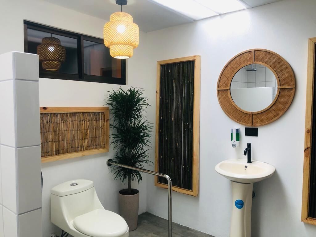 Casa de banho com sanita, lavatório e espelho com estrutura de fibra vegetal.
