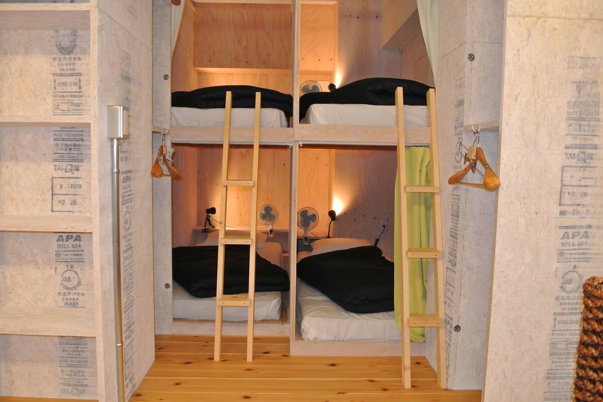 Quarto com beliches, paredes de madeira, uma escada e dois ventiladores.