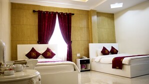 Quarto de hotel com duas camas, mesa de cabeceira e janela com cortinas.