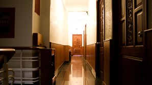 Um corredor estreito e bem cuidado, com portas de madeira e uma escada à esquerda.