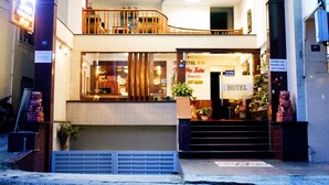 Um hotel com letreiro de neon, uma escadaria que leva à entrada e uma porta de acesso visível.