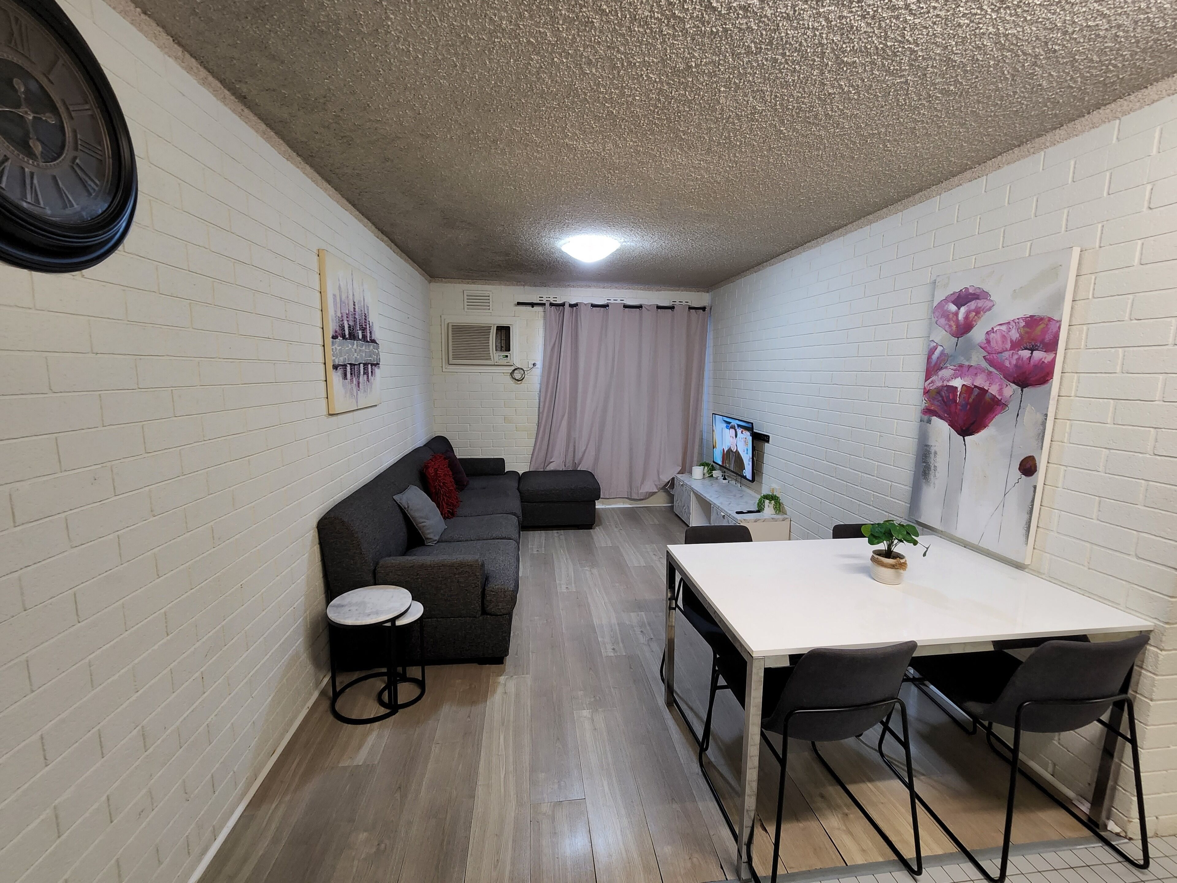 Um espaço de estar compacto com sofá, uma pequena mesa redonda, uma mesa de jantar com cadeiras, televisão e um quadro de flores na parede.