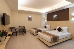 Quarto de hotel com duas camas, uma escrivaninha, cadeiras, televisão e obras de arte nas paredes.