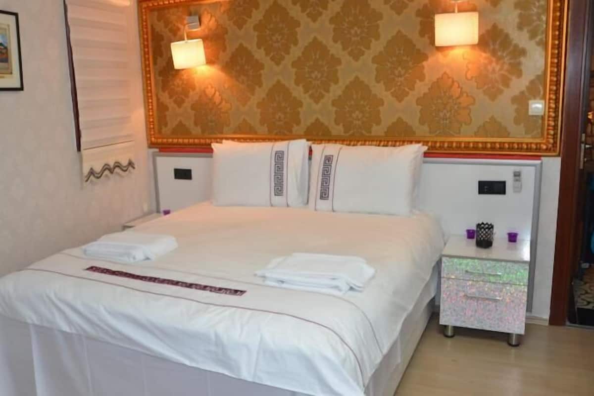 Quarto de hotel com cama grande, duas mesas de cabeceira, radiador e um quadro na parede.