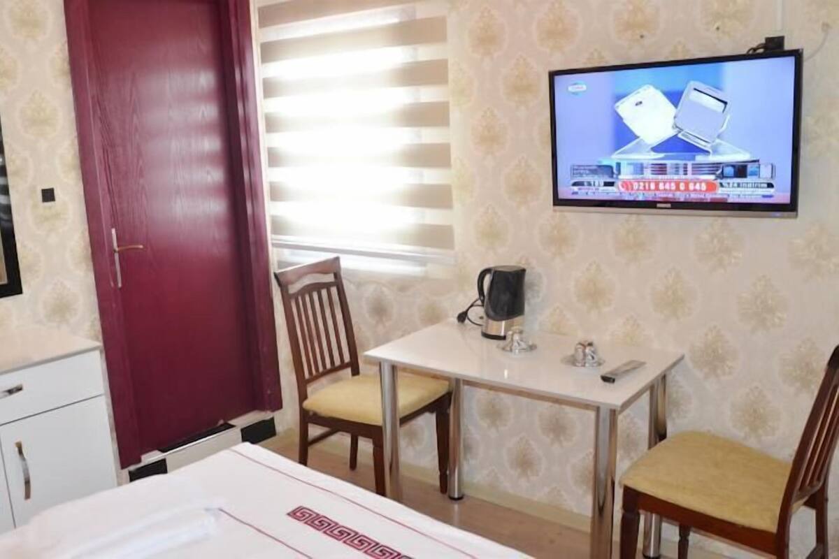 Quarto de hotel com cama, escrivaninha, cadeira, televisão e armário.