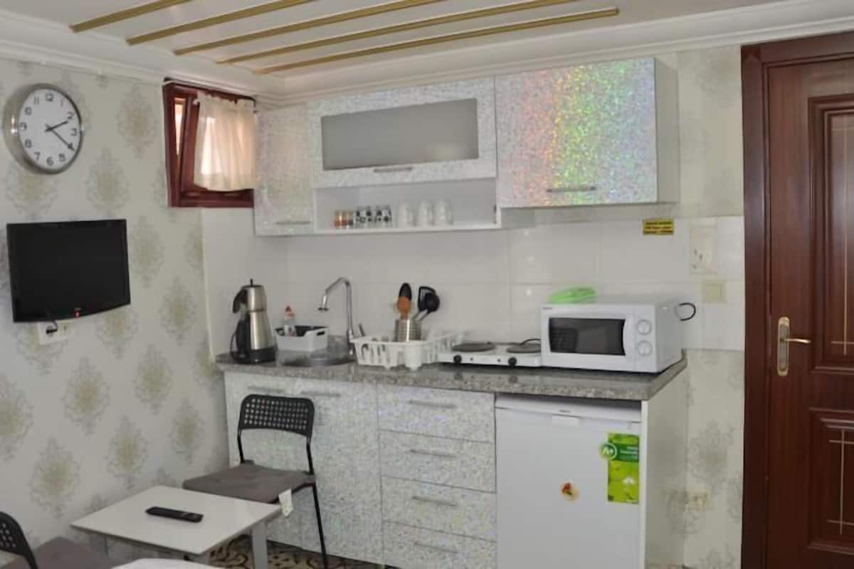 Uma cozinha compacta com micro-ondas, chaleira e um pequeno espaço de refeições com uma cadeira e mesa.