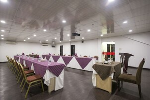 Uma sala de conferências com mesas preparadas para uma reunião, equipada com cadeiras e um pódio.