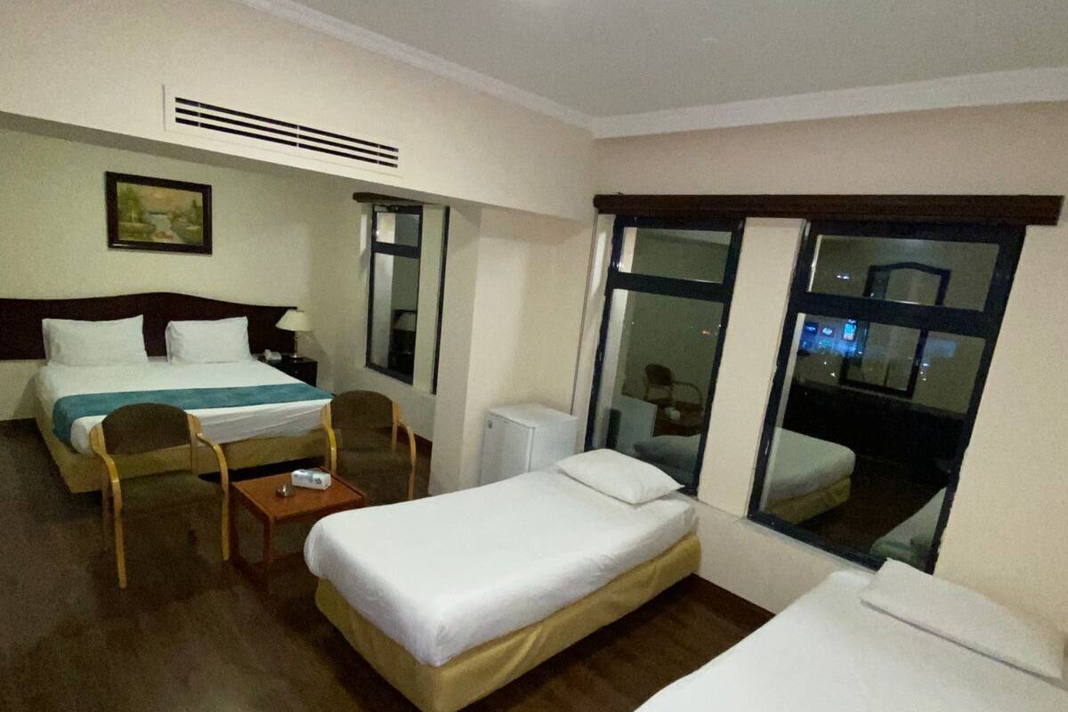 Quarto de hotel com duas camas de solteiro, um sofá-cama, uma escrivaninha, uma cadeira e uma janela com vista.