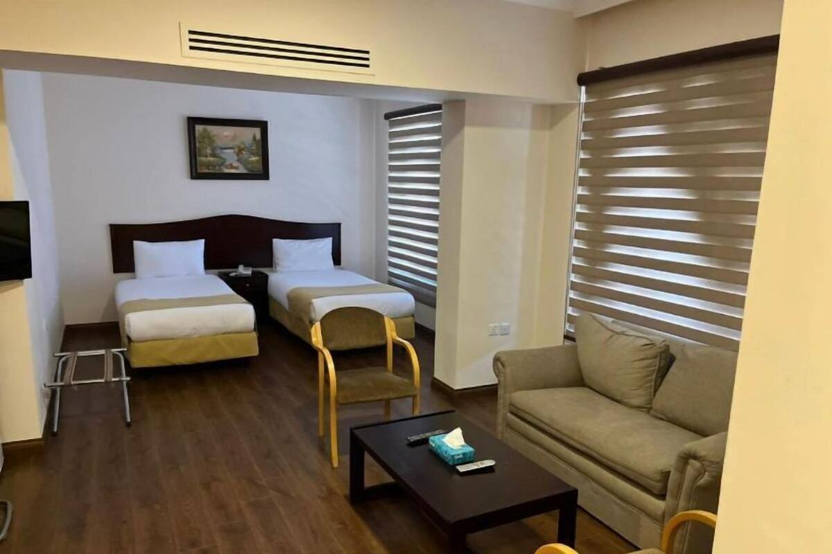 Quarto de hotel com duas camas de solteiro, um sofá, uma mesinha e uma cadeira.