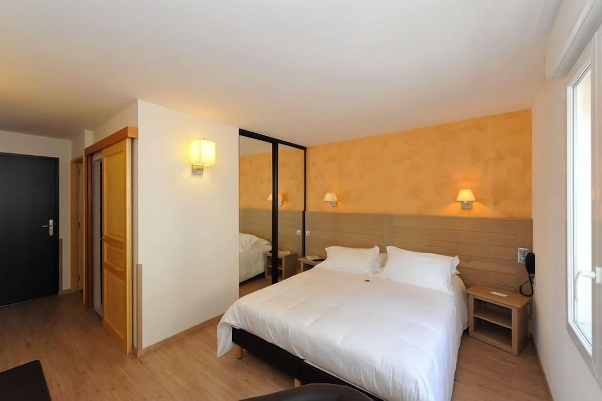 Quarto de hotel com cama, mesas de cabeceira, espelho e janela.