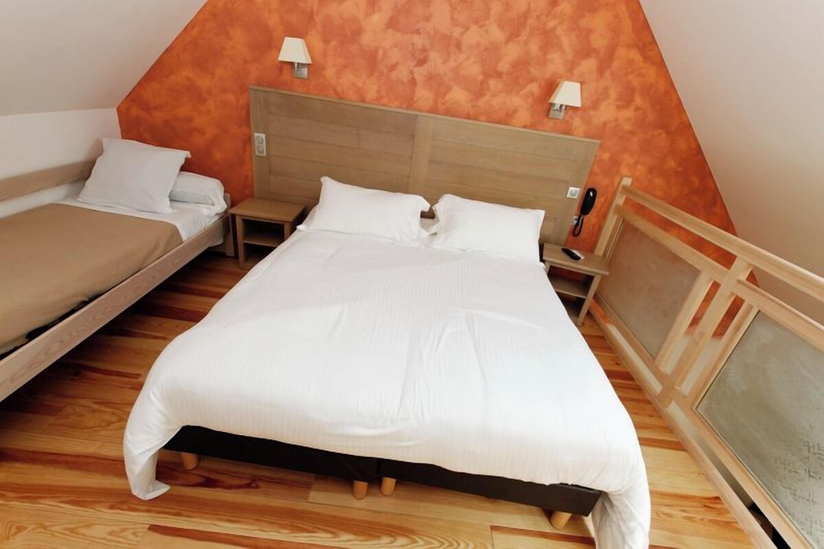 Quarto com duas camas, piso de madeira e teto inclinado.