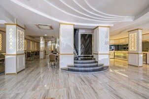 Um hall amplo com piso de mármore, uma escadaria central e uma área de recepção com design moderno.