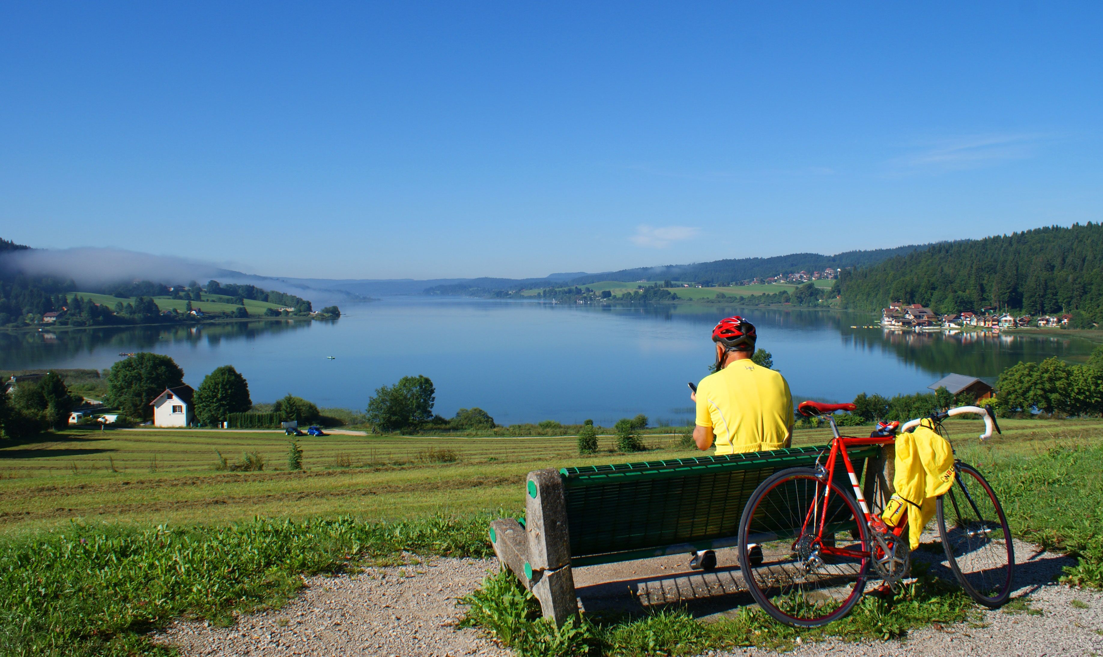 Um lago com um banco e uma bicicleta, cercado por vegetação e casas.