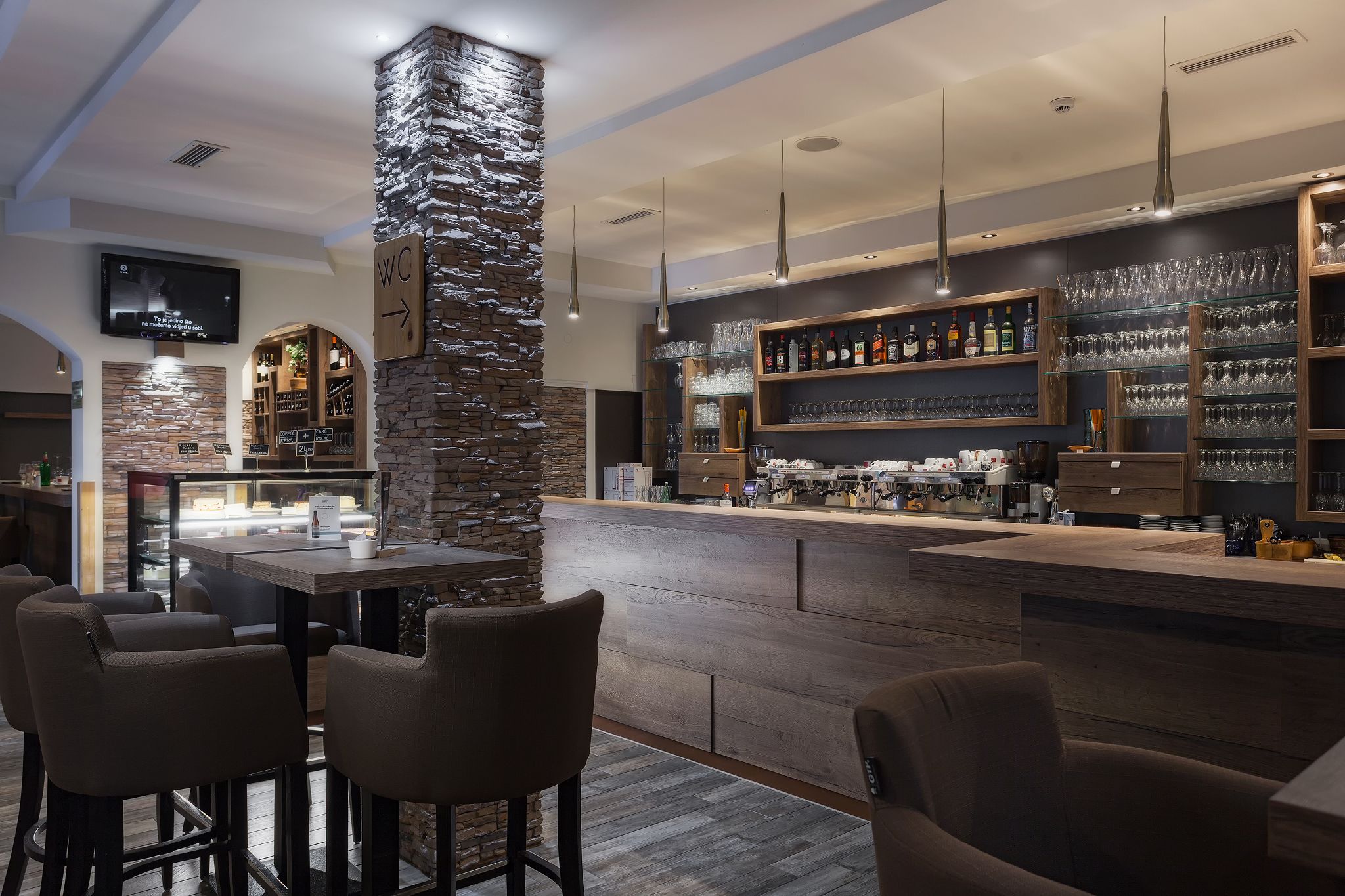 Uma área de bar moderna com parede de destaque em pedra, balcão de madeira e assentos com banquetas.