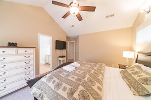 Quarto com cama, cômoda, ventilador de teto, televisão e abajur.