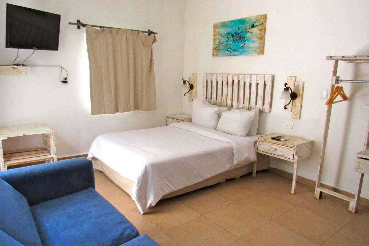 Quarto com cama, sofá azul, televisão, quadro e cabeceira de madeira.
