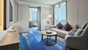 Quarto de hotel moderno com sofá, mesa de centro redonda, escrivaninha e vista para o mar.