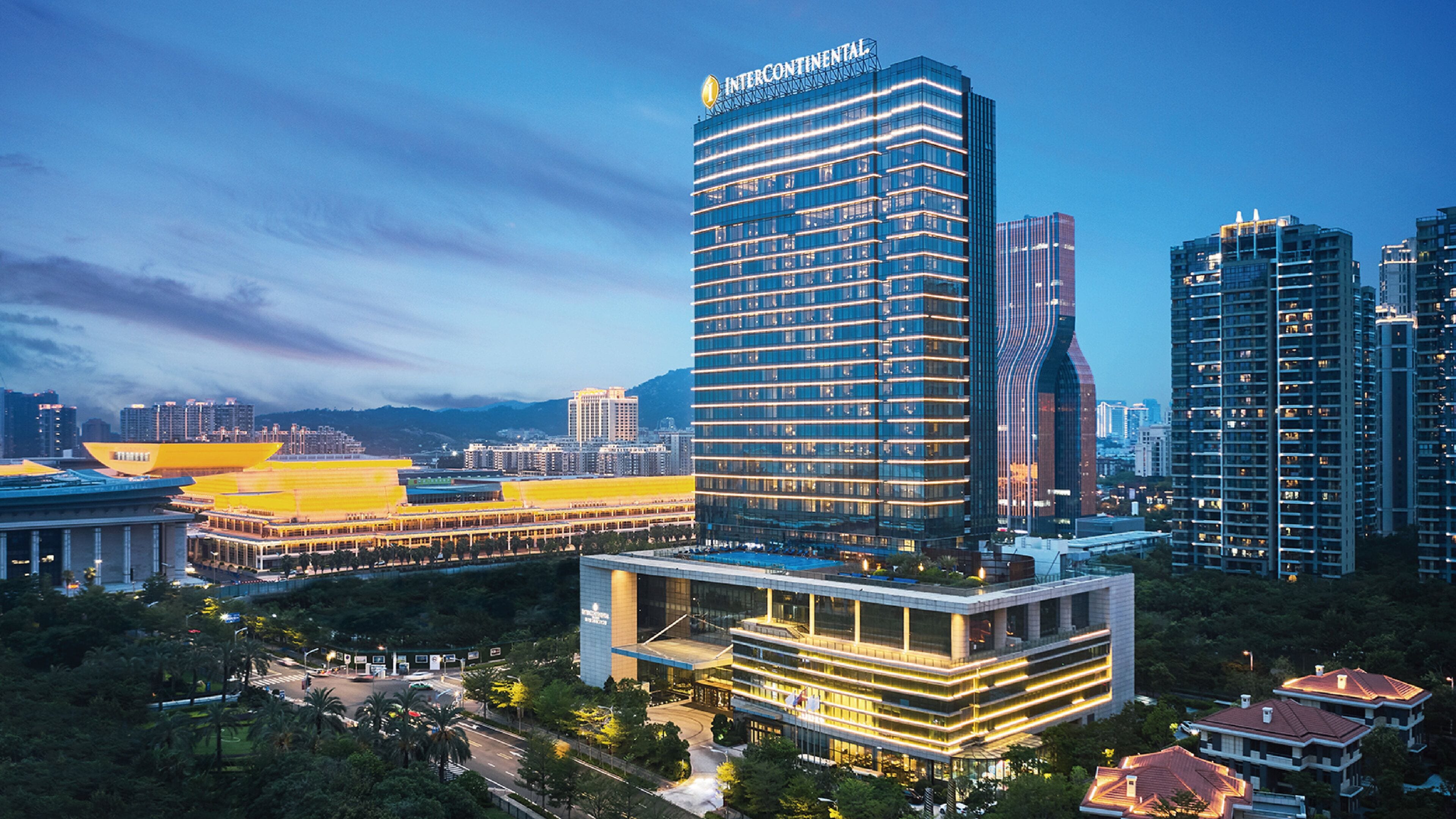 Um hotel moderno com o logotipo InterContinental bem visível, rodeado por edifícios altos e um ambiente urbano iluminado.