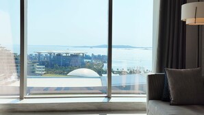 Quarto de hotel moderno com uma grande janela que oferece vista para um horizonte costeiro, incluindo uma estrutura de cúpula branca marcante.