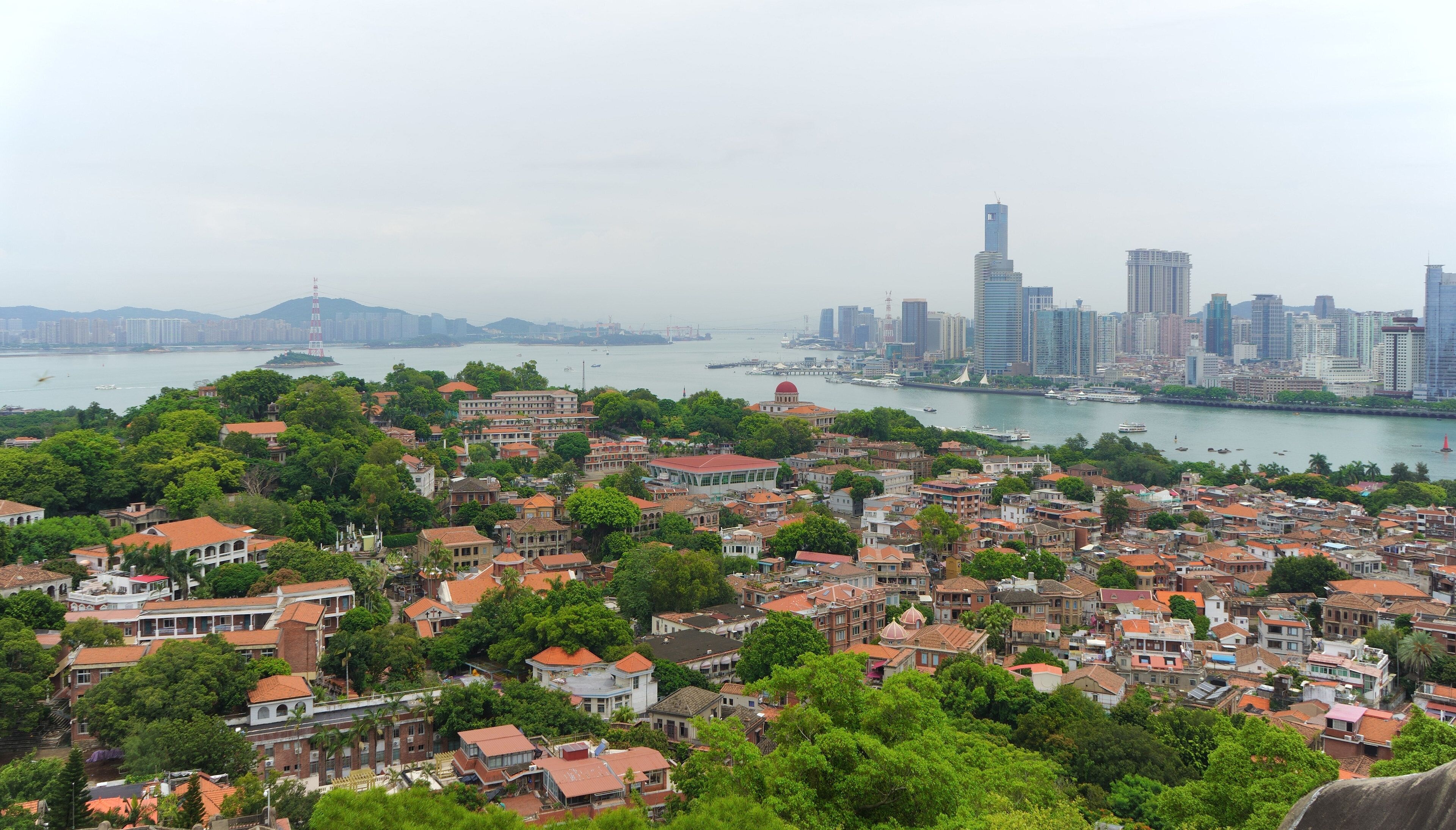Uma área urbana densamente povoada, com uma mistura de edifícios antigos e modernos, um rio com barcos e um horizonte urbano distante.