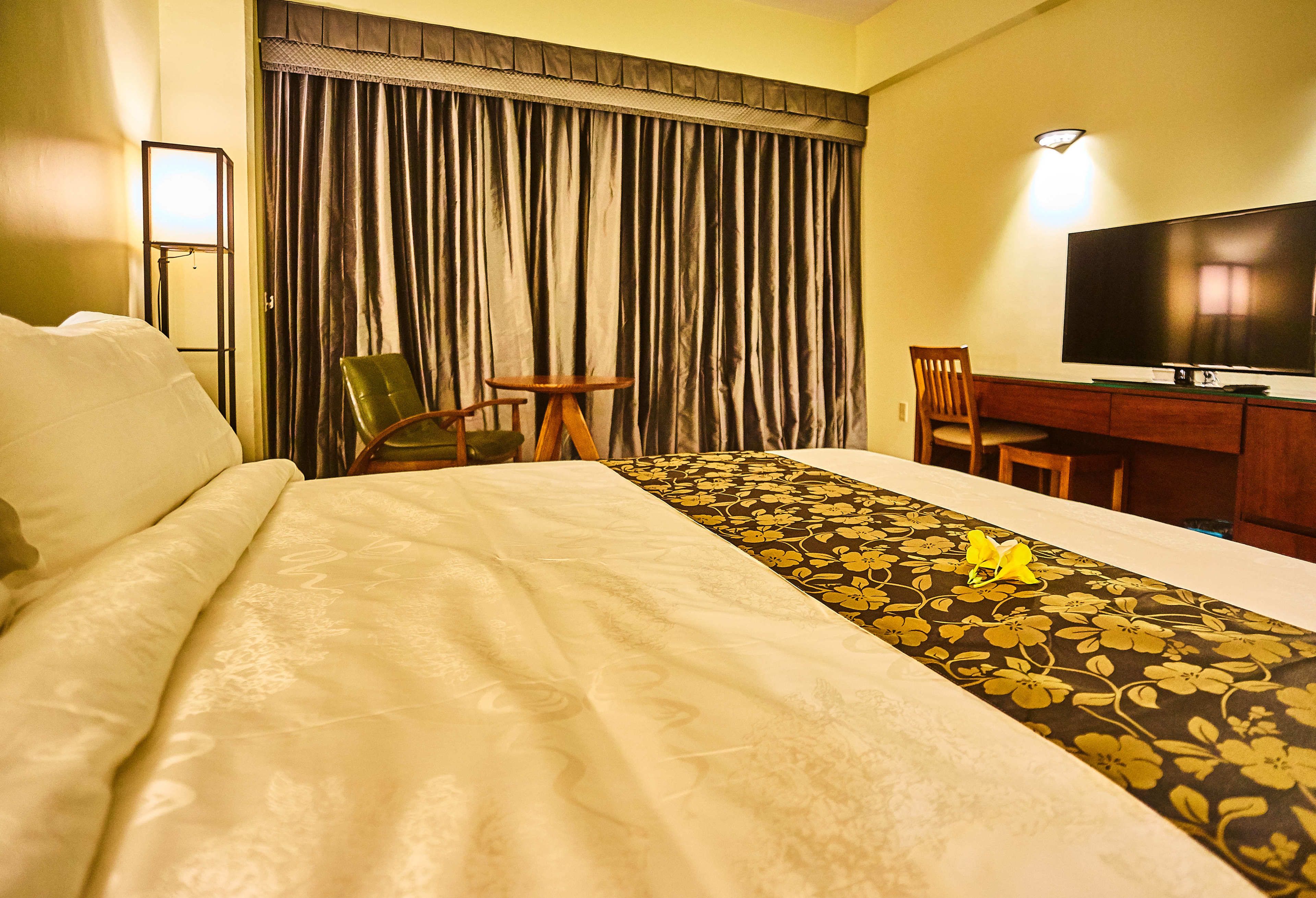 Quarto de hotel com uma cama grande, uma mesa com televisão, uma cadeira e uma cortina.