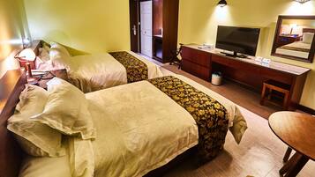 Quarto de hotel com duas camas, uma escrivaninha, uma televisão e um espelho.