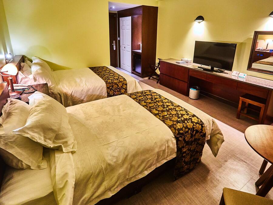 Quarto de hotel com duas camas, uma escrivaninha, uma televisão e um espelho.