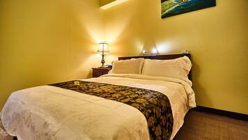Quarto de hotel com cama, mesa de cabeceira, abajur e um quadro na parede.