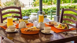 Mesa de pequeno-almoço montada ao ar livre, com diversas opções de comida e bebidas.