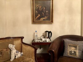 Quarto com um sofá antigo, uma pequena mesa lateral de madeira com uma chaleira e um quadro pendurado na parede.