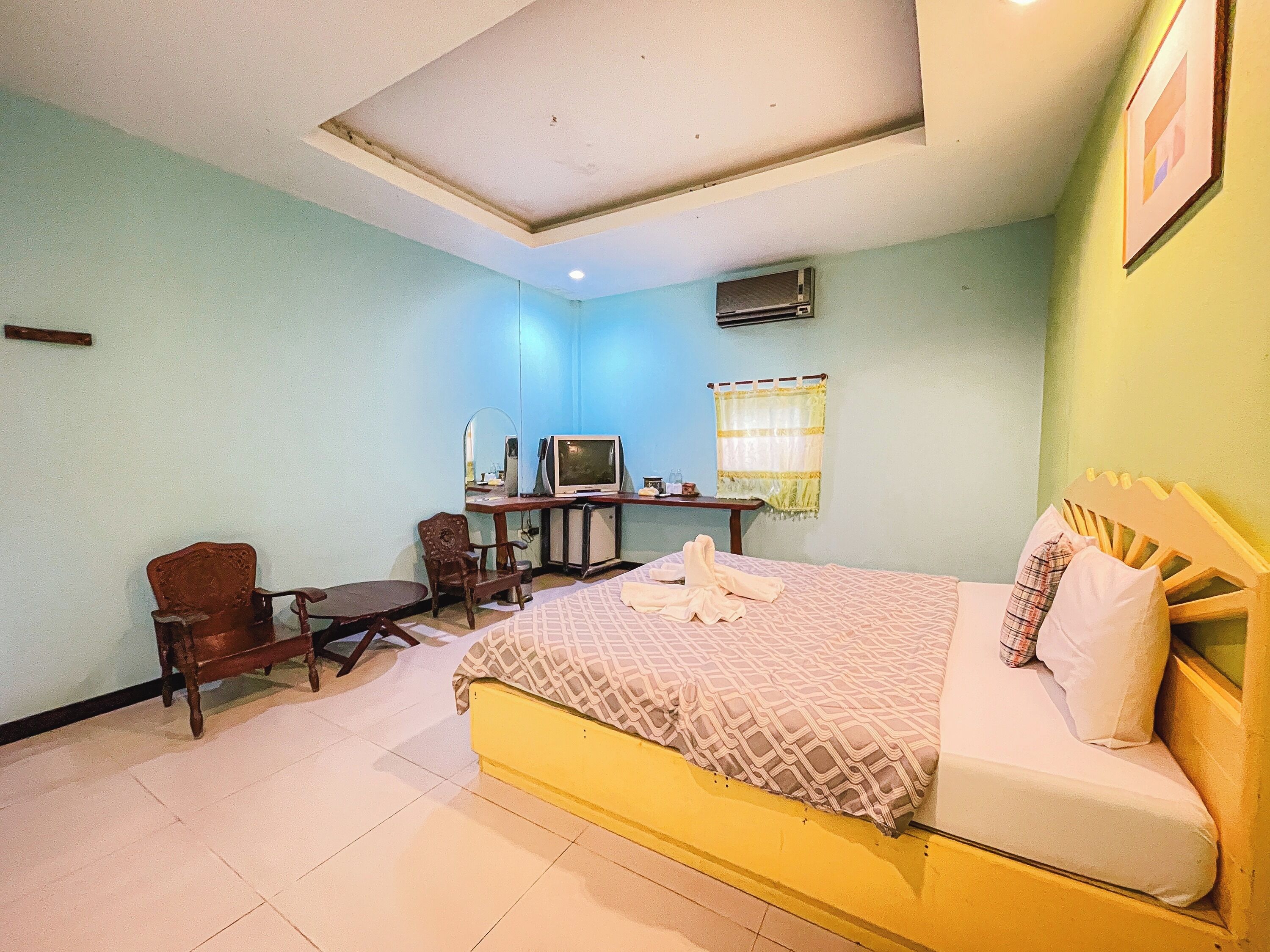 Quarto de hotel com uma cama, uma escrivaninha com computador, uma cadeira e uma televisão.