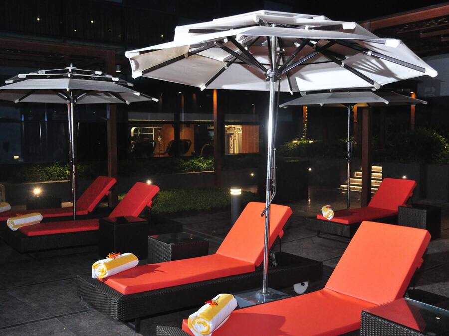 Uma área de estar no terraço com poltronas vermelhas e guarda-sóis brancos.