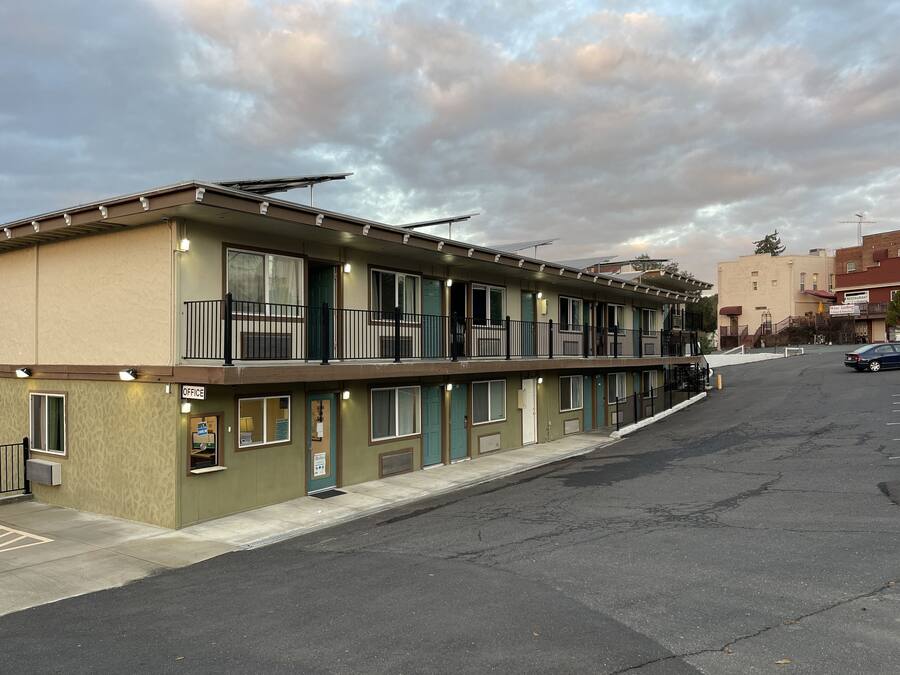 Um motel de vários andares com telhado plano, grandes janelas e estacionamento.
